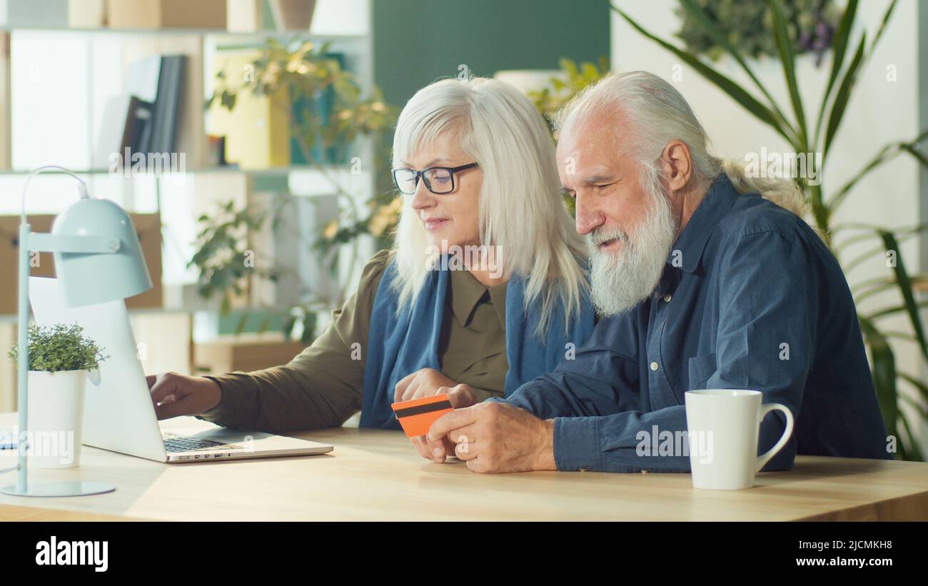 Happy Elderly Couple Shopping Online From Home Using Computer And