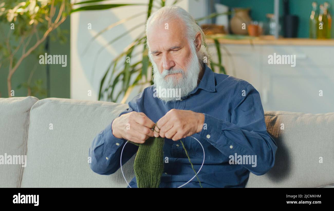 A Concentrated Elderly Man Knits While Sitting on a Sofa in His Cozy ...
