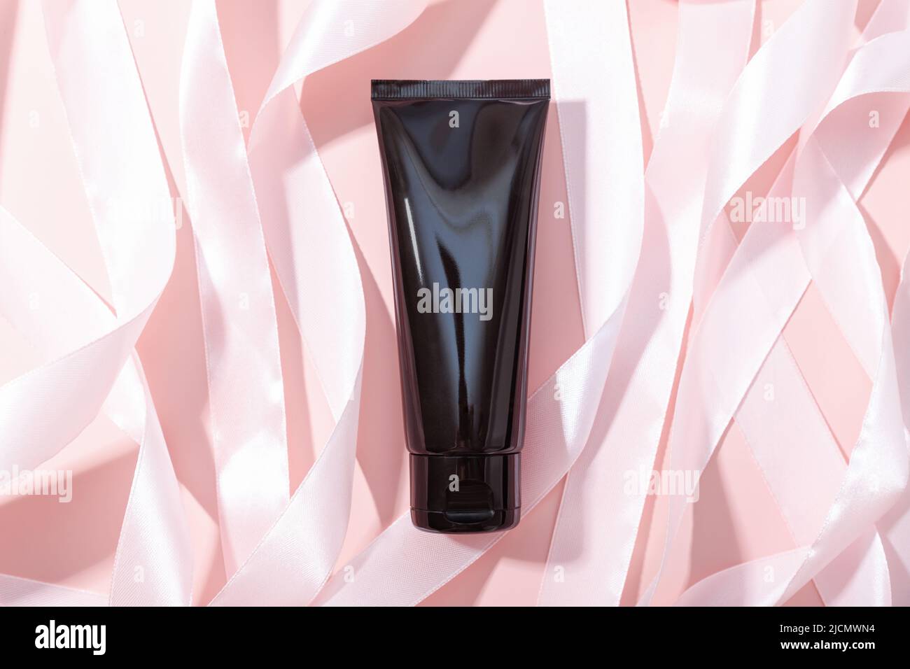 Black squeeze bottle cosmetic tube and pink ribbons on pink background ...
