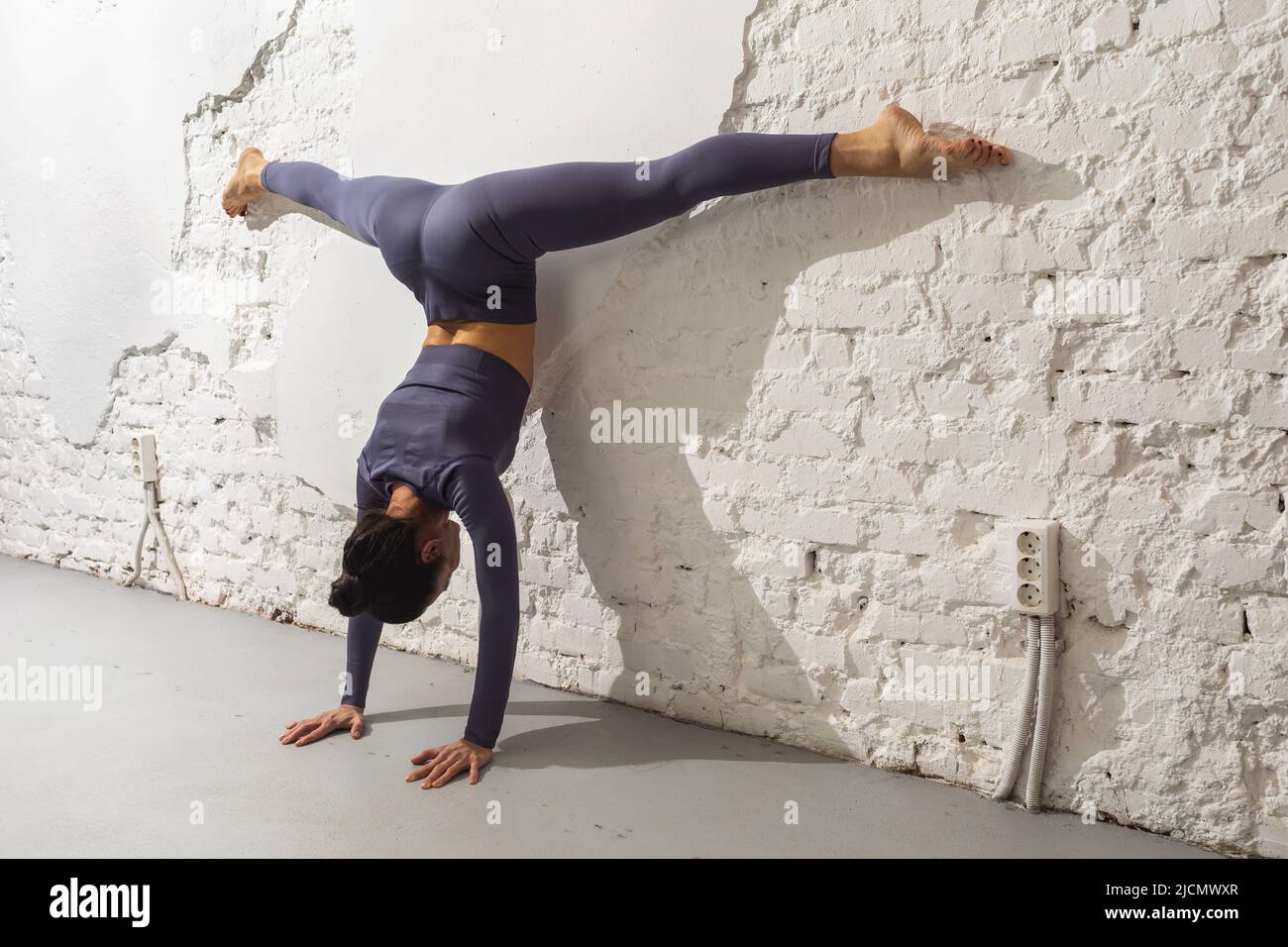 A female yoga practitioner performs the Adho Mukha Vrikshasana exercise with Samakonasana, two ...