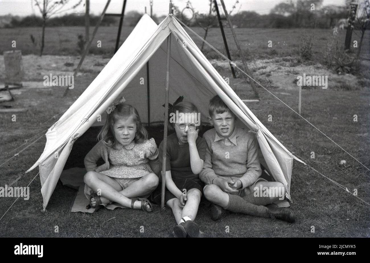 1950s, historical, outside in a grass area of a playground, three young ...