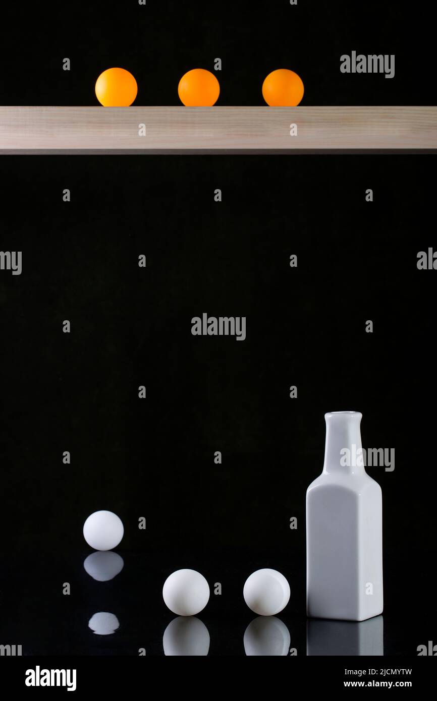 Still life with a white vase and white and yellow balls on a black ...