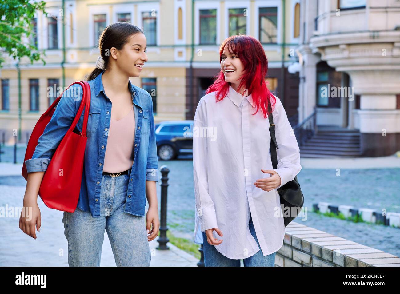Two walking talking laughing teenage girls walking down the city street ...