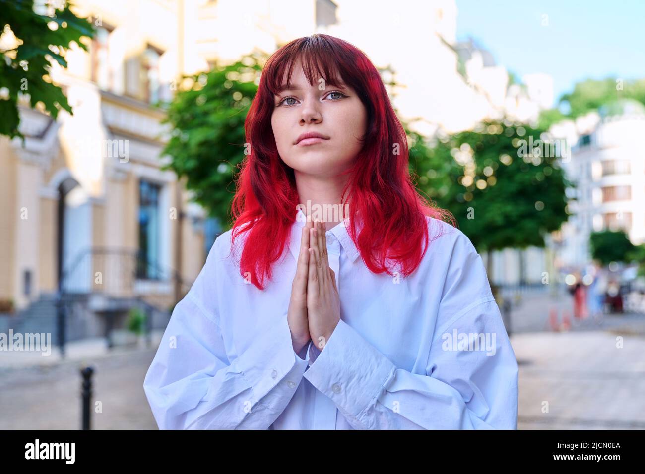 Young teenage female folded her hands in prayer, outdoor in the city ...