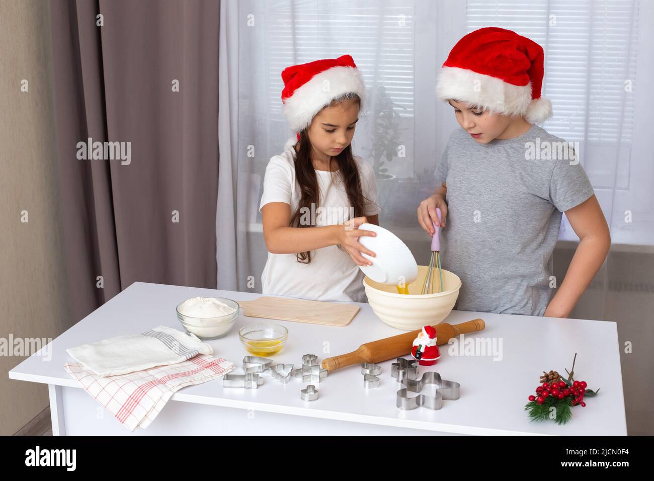 Children in red caps, stand at a white kitchen table, prepare Christmas ...