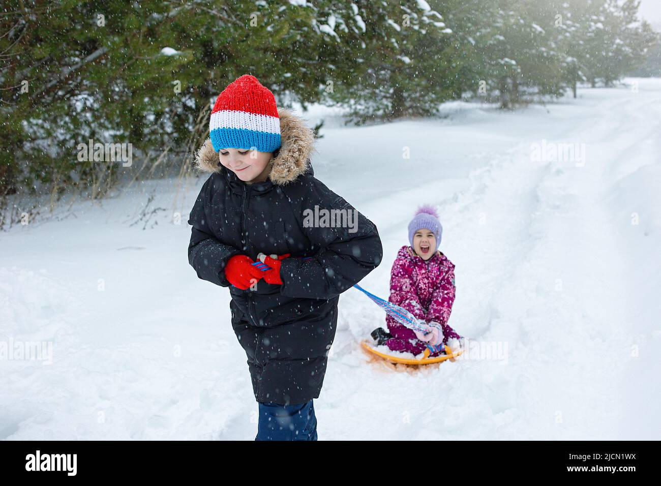 A teenage boy rolls a little girl in the snow on a plastic ice rink ...