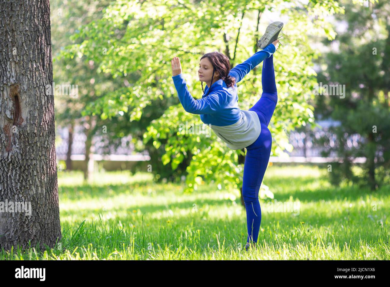 A 35 year old woman practices yoga in a city park. She does a balance exercise while standing on ...