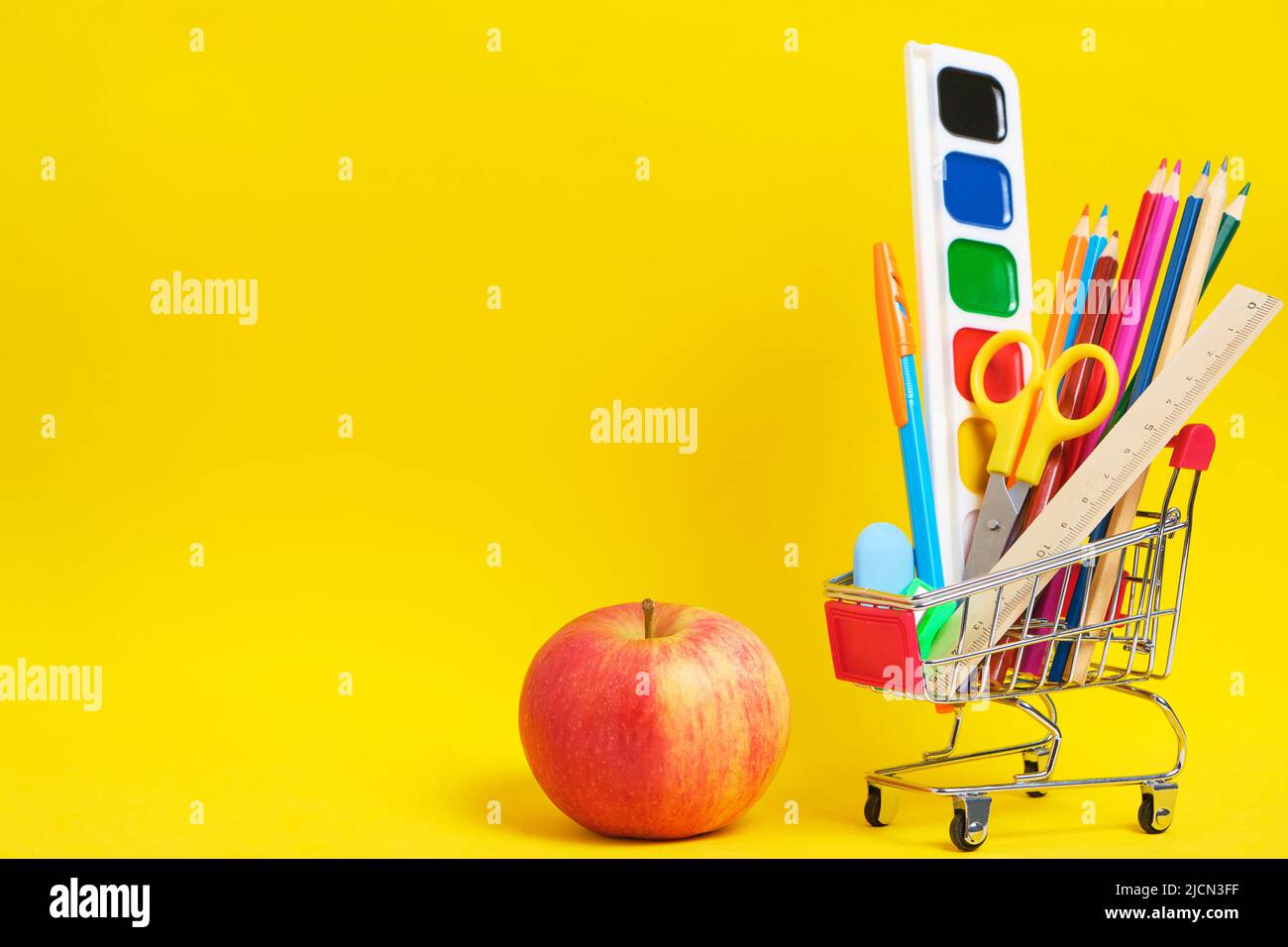 Apple, stationery and school supplies in a shopping cart, yellow ...