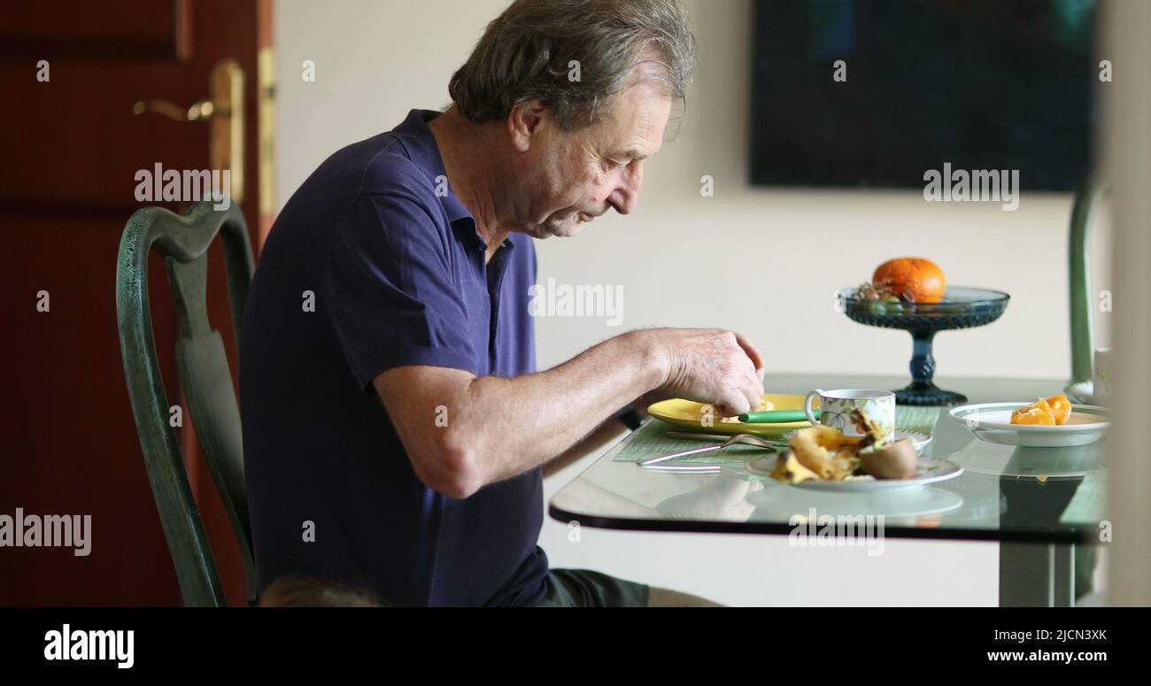 Grandfather eating breakfast. Infant child wanting attention standing ...
