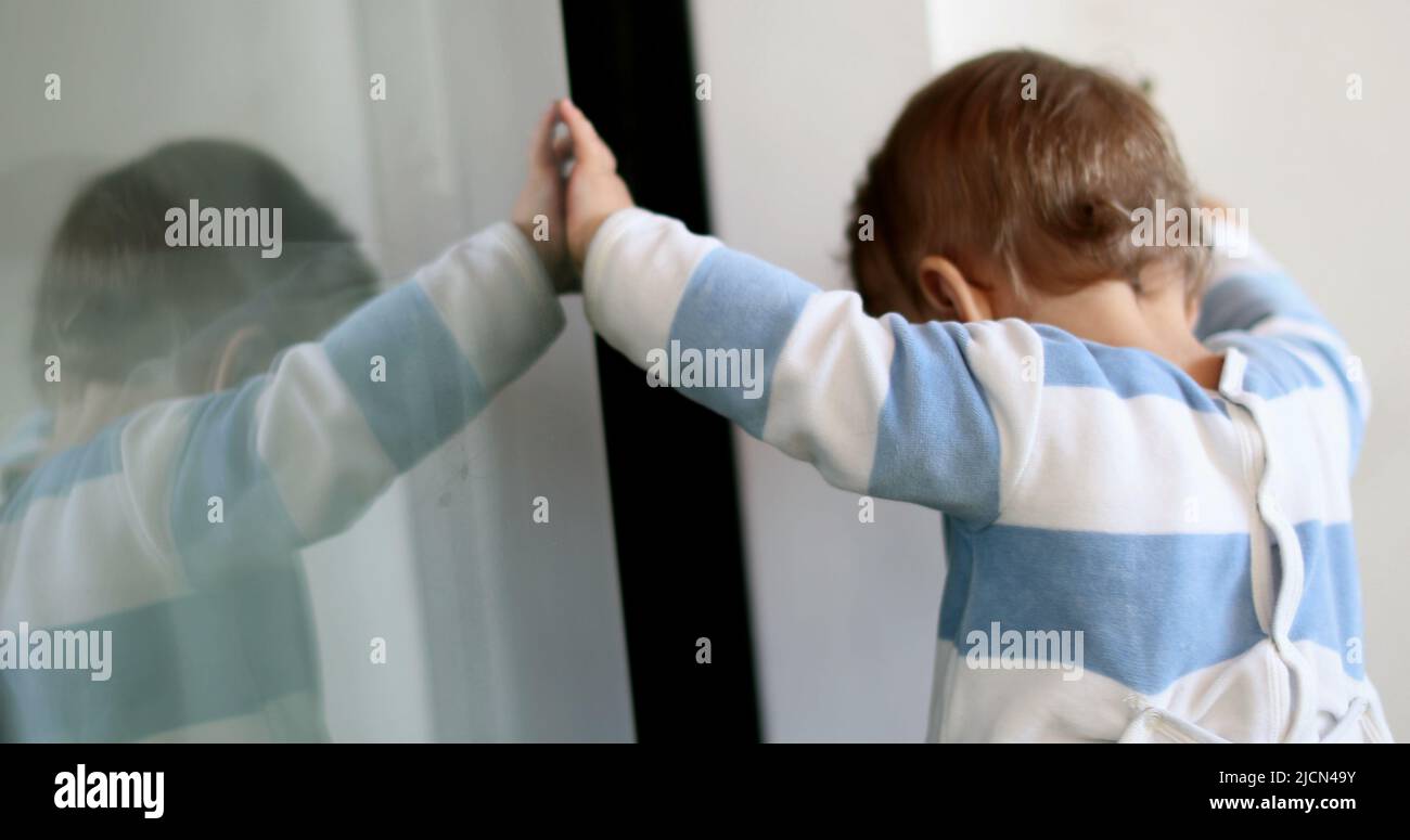 Toddler boy leaning on window reflection. Baby infant standing to ...