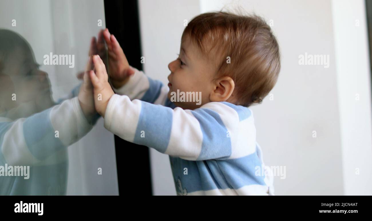 Toddler boy leaning on window reflection. Baby infant standing to ...