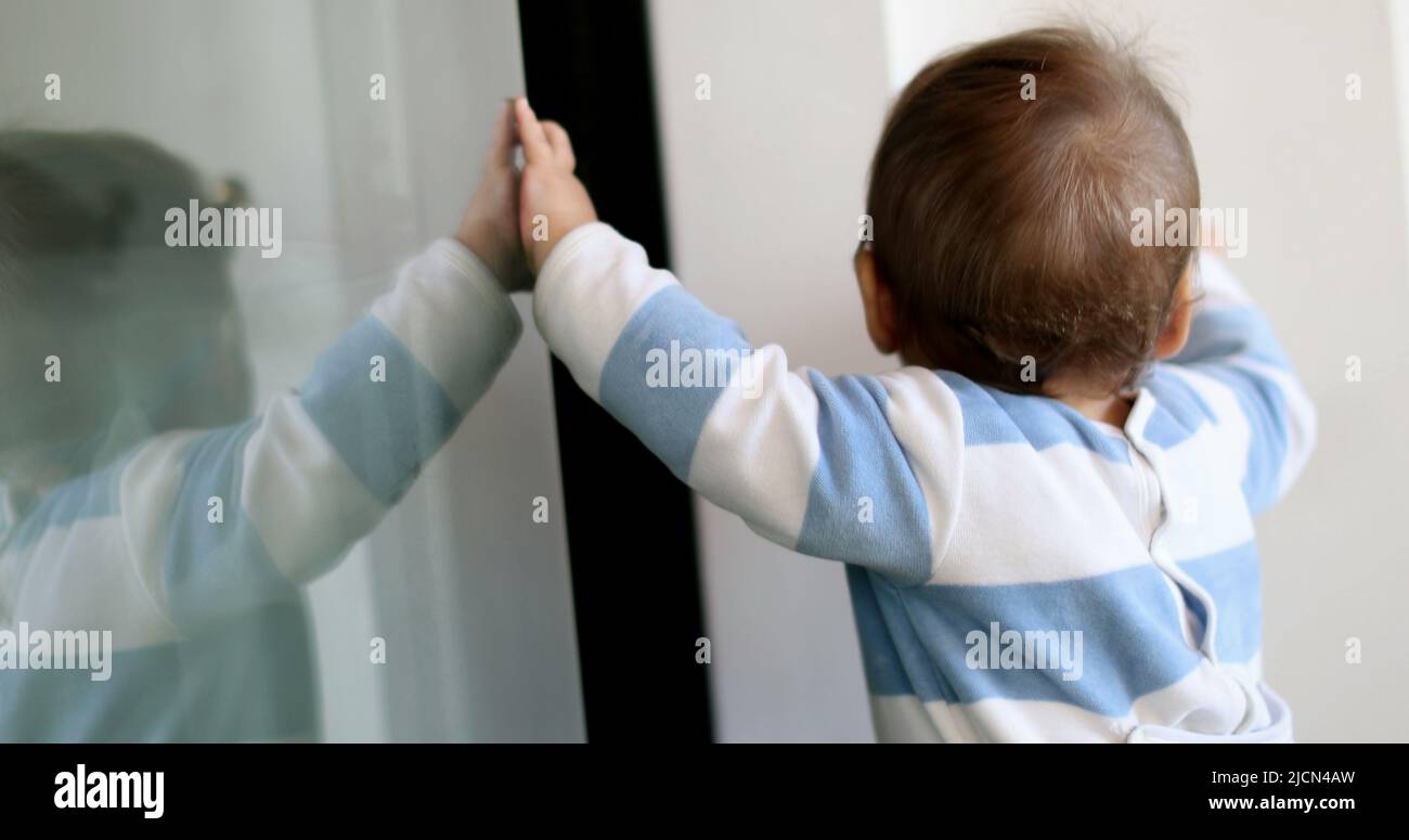 Toddler boy leaning on window reflection. Baby infant standing to ...