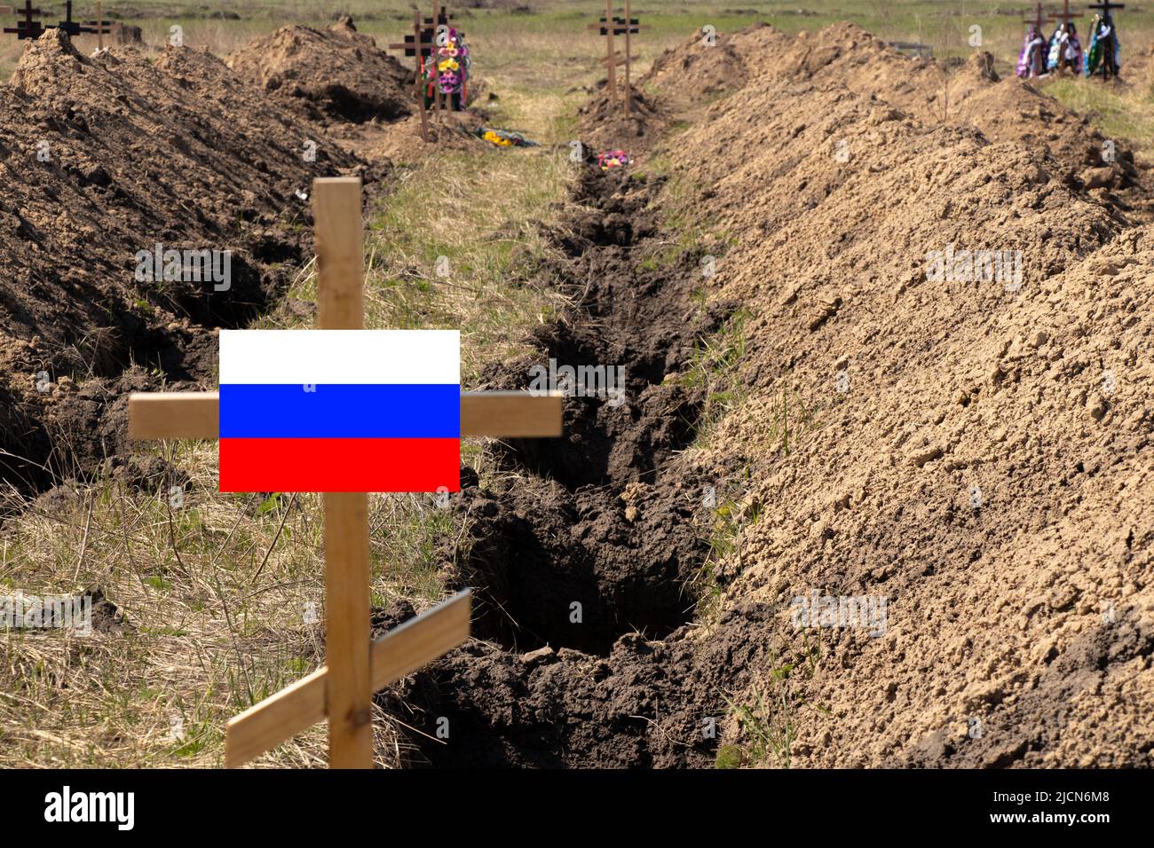 Freshly dug new graves and a wooden cross with the flag of Russia, a ...