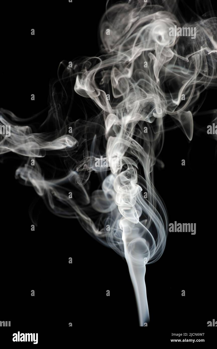 Puffs and curls of white smoke against a black background rising from a ...