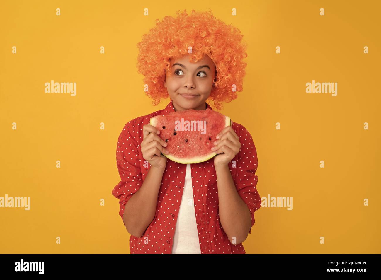 happy child in fancy orange hair wig hold fresh ripe water melon slice ...