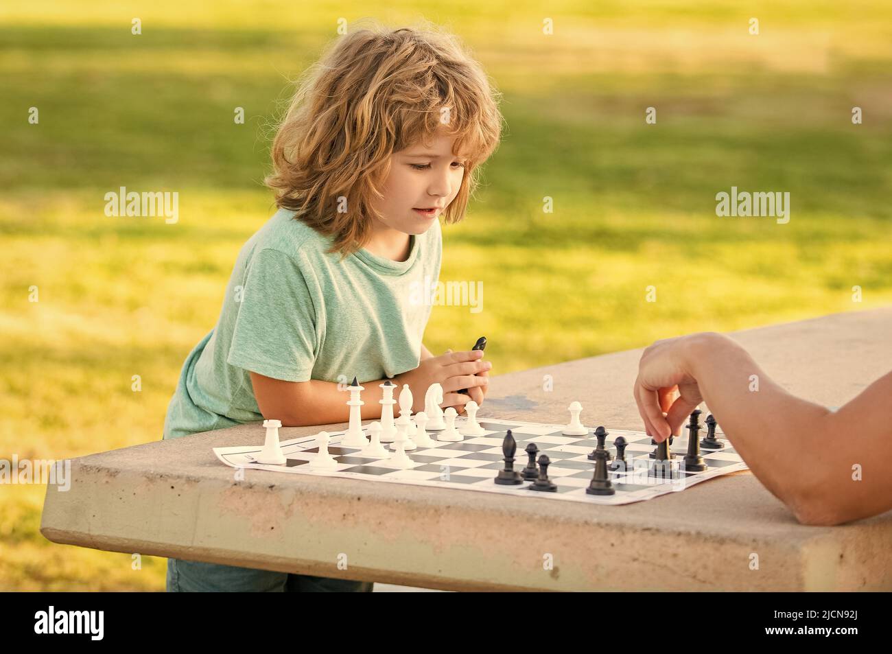 son kid playing chess on table in park outdoor with his father ...