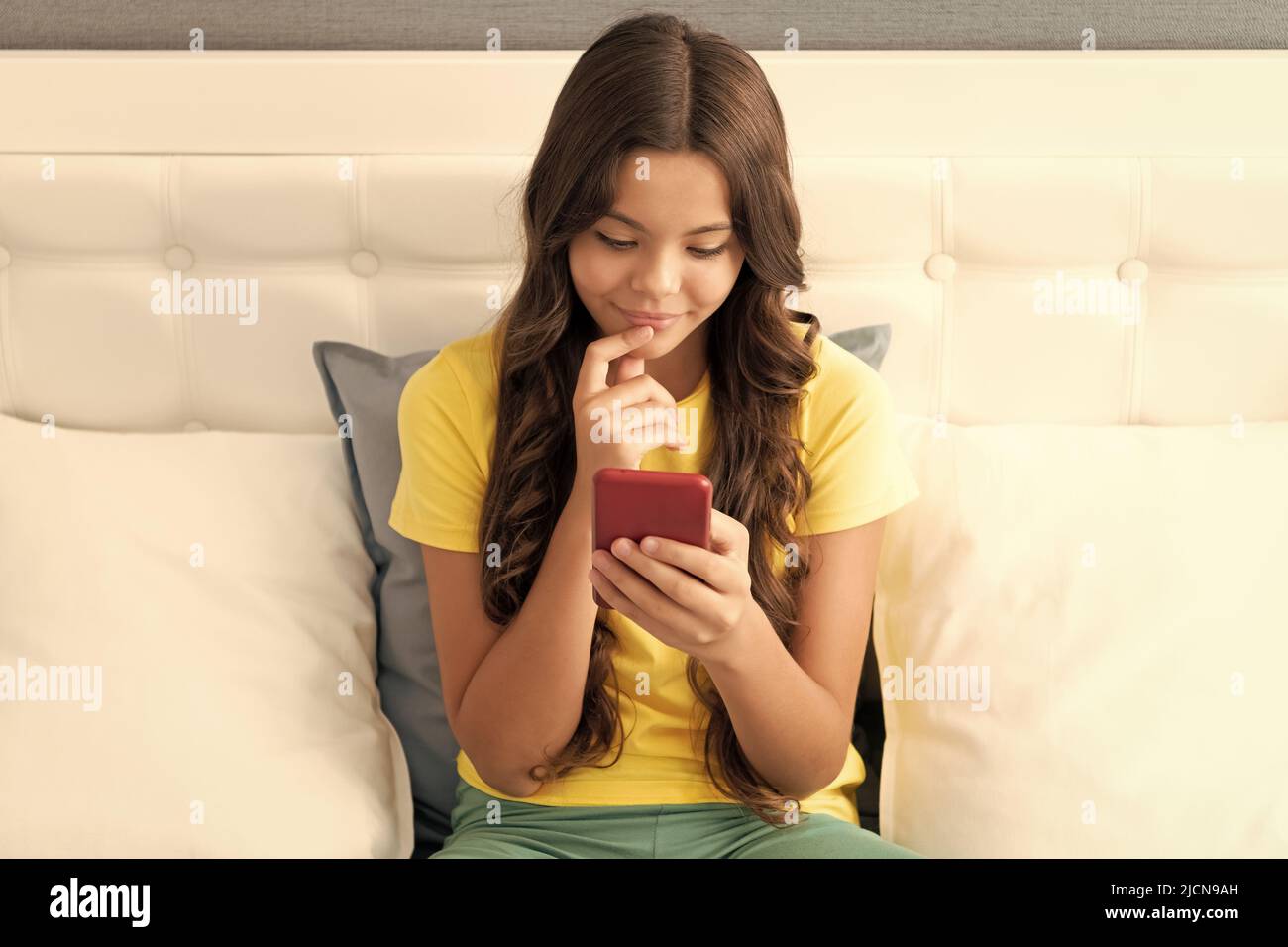 Happy girl child smile chatting on mobile phone while sitting on bed ...