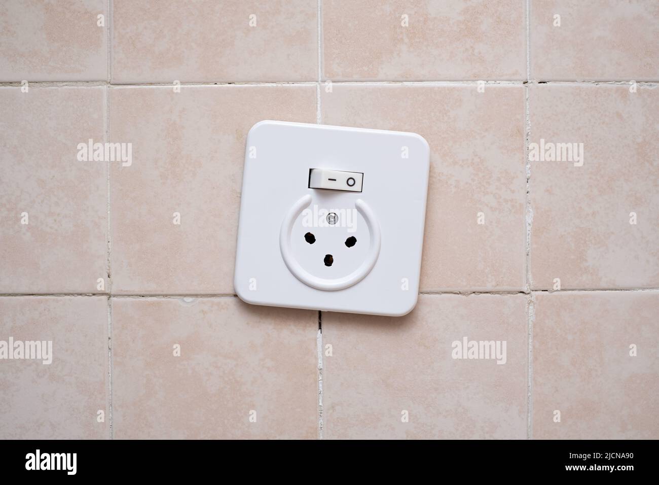 Crookedly mounted electrical socket with switch. On ceramic tile in ...