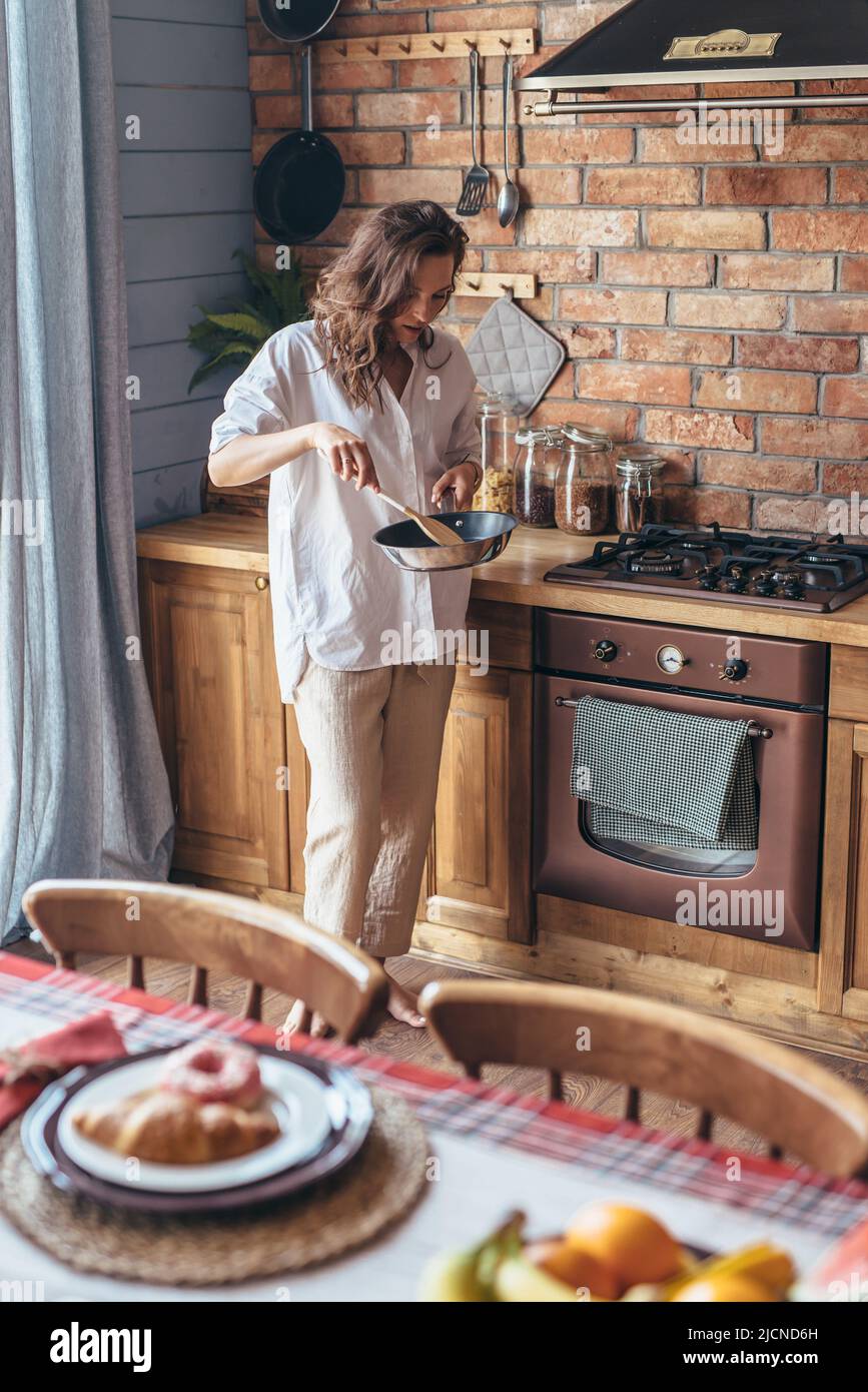 Woman in the kitchen at the stove stirring food in a frying pan Stock ...