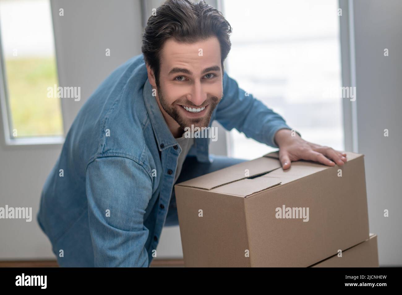 Man bending over boxes smiling at camera indoors Stock Photo - Alamy