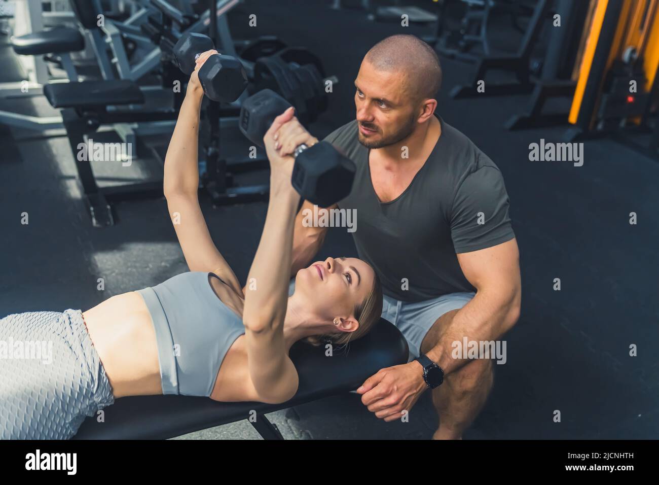 European blonde sportswoman lifting dumbbells at a gym. Bald ...