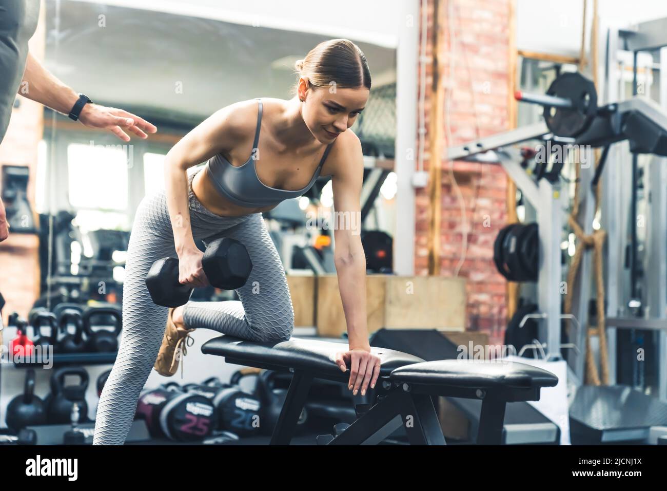Caucasian millennial athletic girl leans with one hand and leg on bench ...