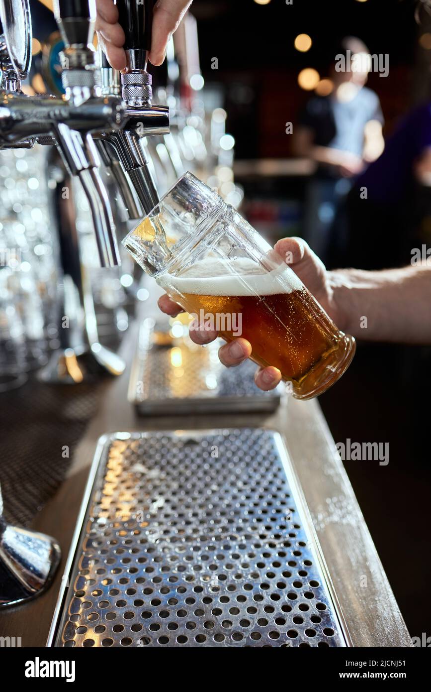 Pouring beer into a mug in a beer bar close-up. Beer bottling in the restaurant. The bar counter ...