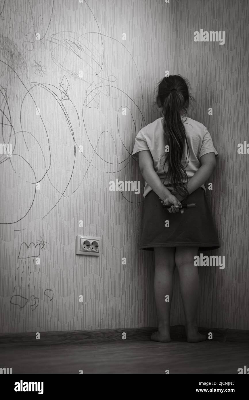 Black And White Portrait Of Little Bad Girl Holding Marker Behind Back Standing Punished In