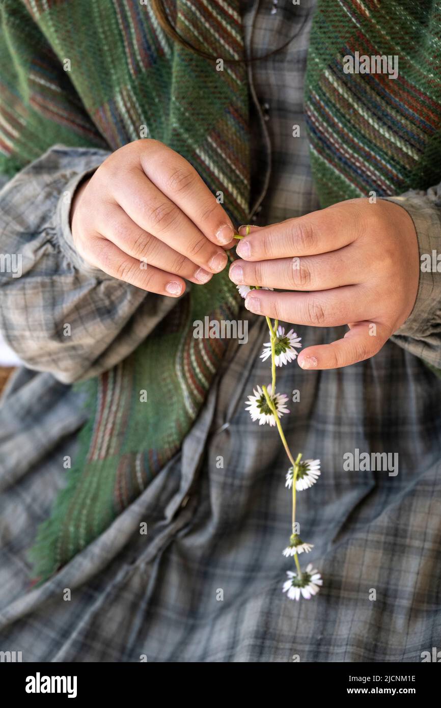 woman making a daisy chain necklace while wearing 1850s historic ...
