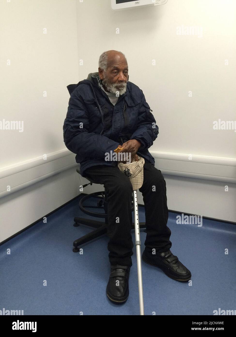 Elderly man sitting down in a hospital waiting room, holding a biscuit ...