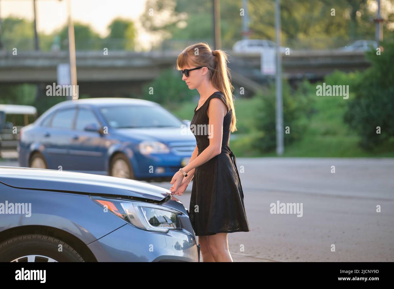 Female driver opening car hood inspecting broken engine on a city ...