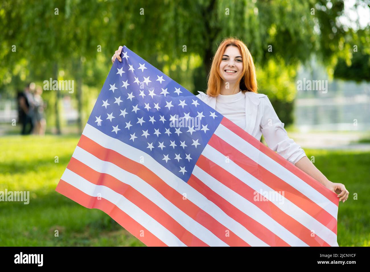 Happy young red haired woman posing with USA national flag standing ...