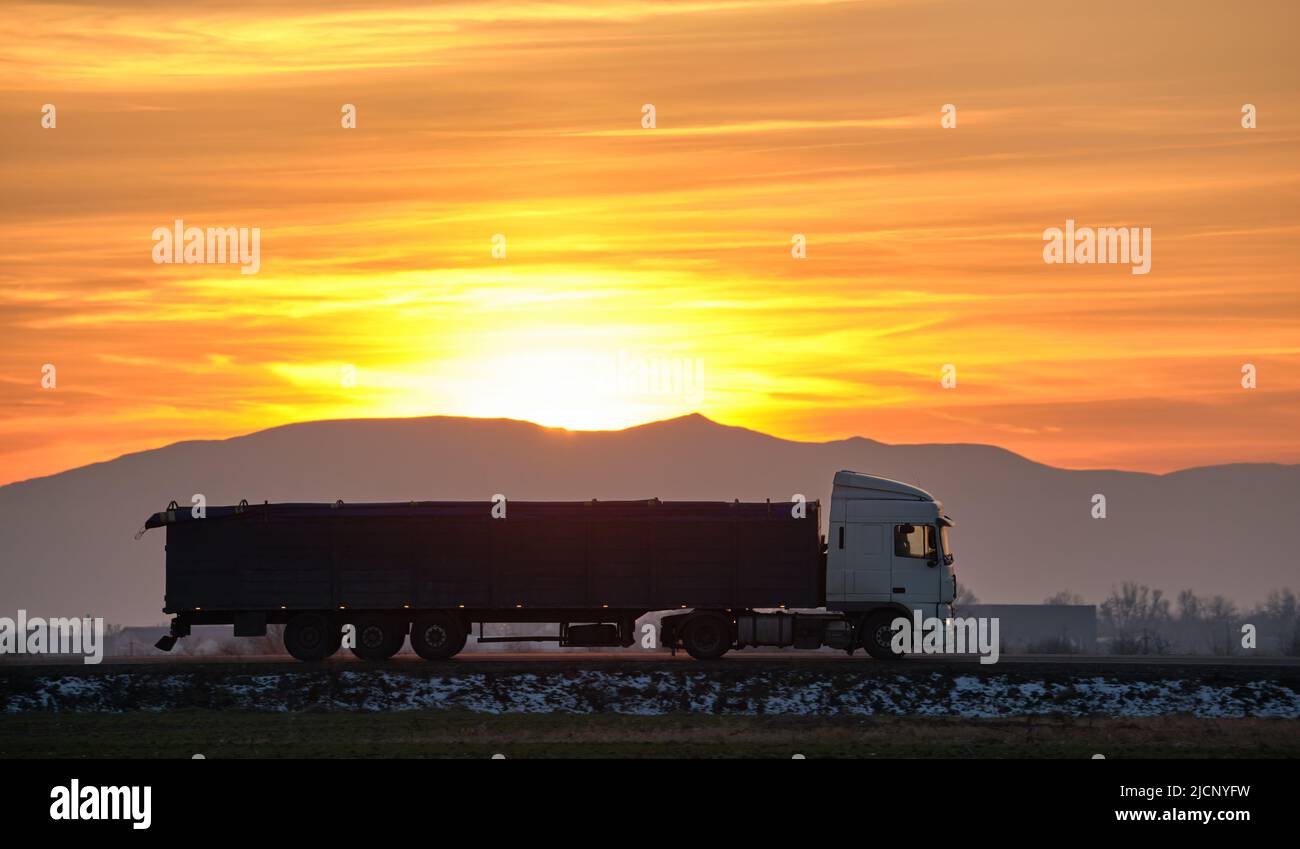 Semi-truck with cargo trailer driving on highway hauling goods in evening. Delivery ...
