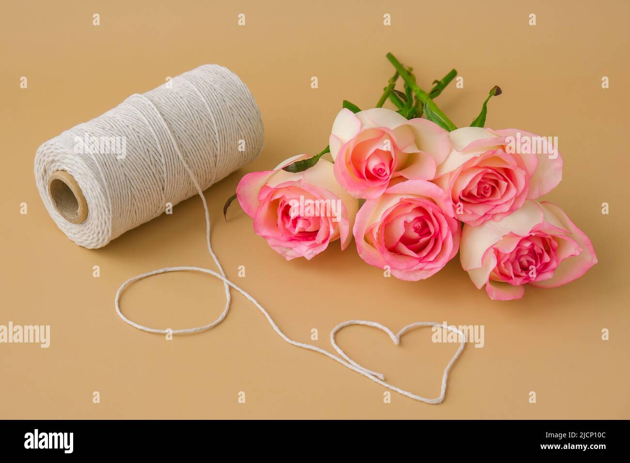 Delicate pink roses with spool of white cotton rope in heart shape on ...