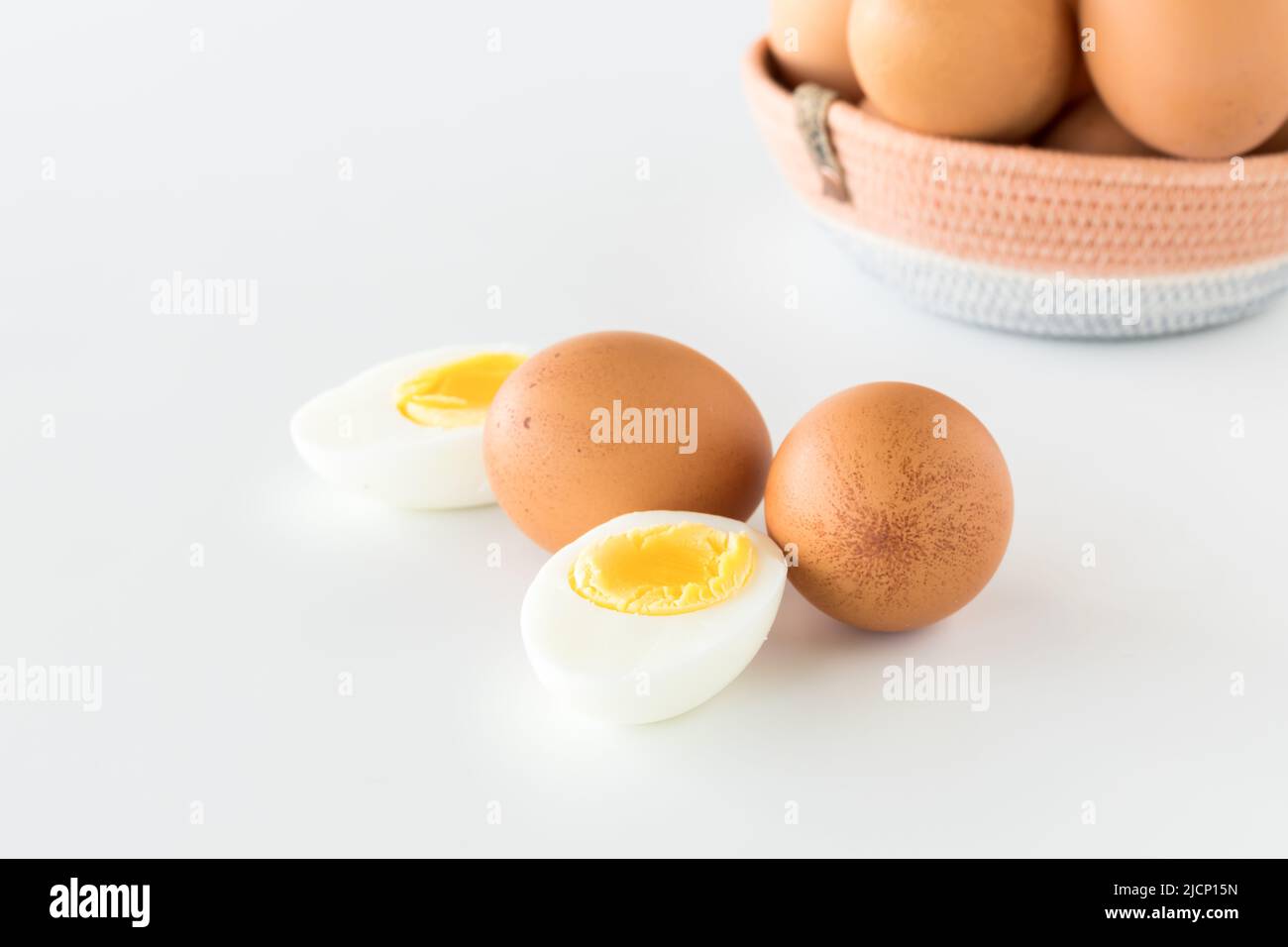 A basket of eggs with two whole eggs in front and one sliced boiled egg ...