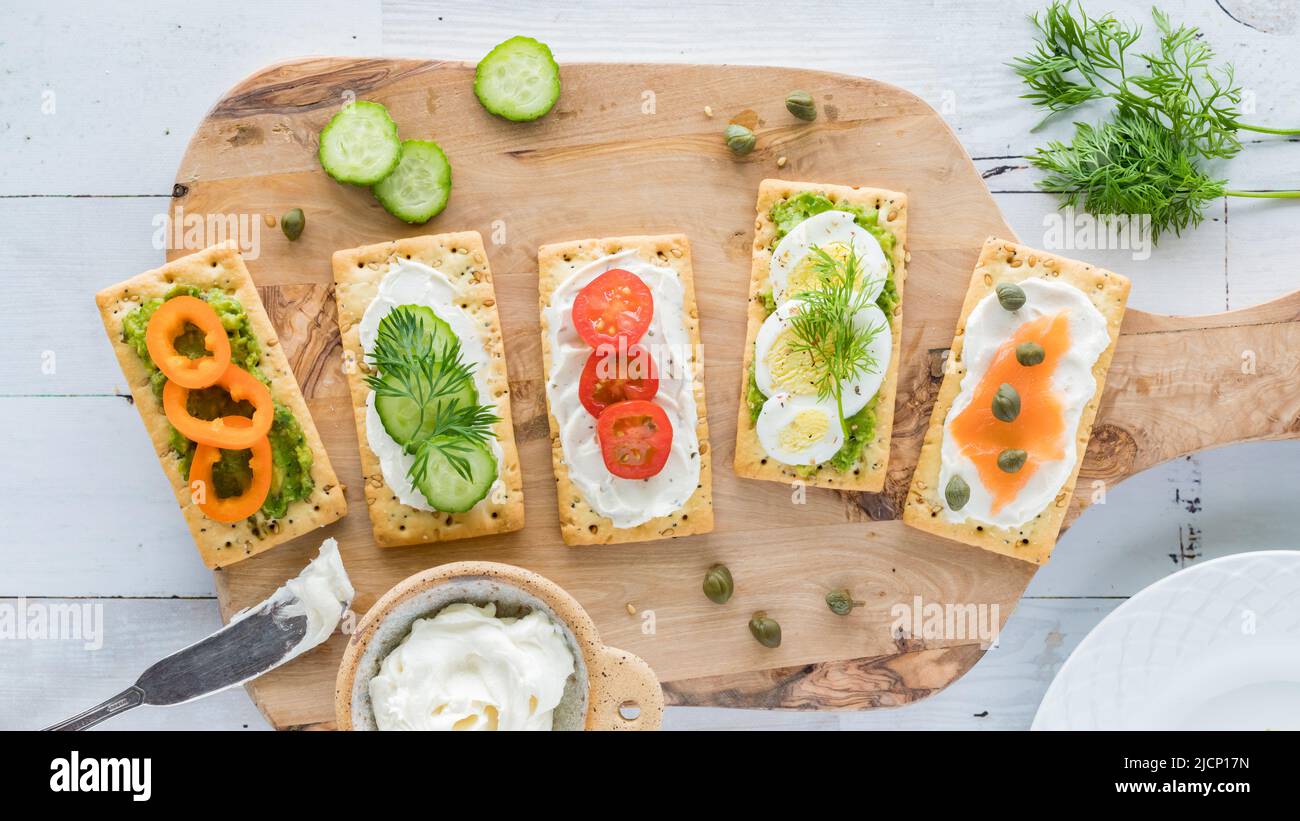 A row of everything crackers with various fresh toppings, on a wooden ...