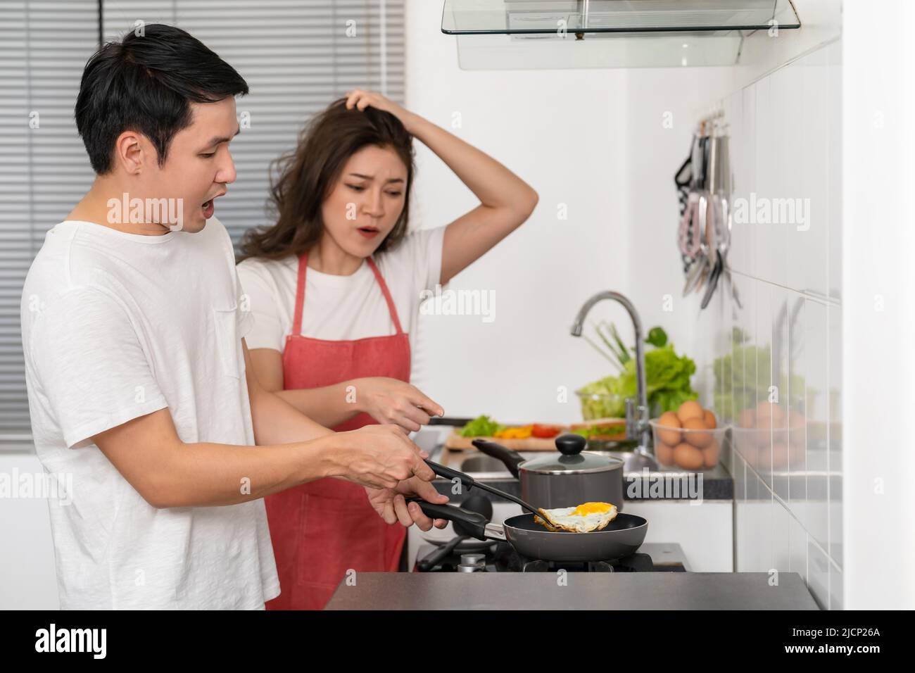 stressed young couple cooking and preparing food in the kitchen at home ...