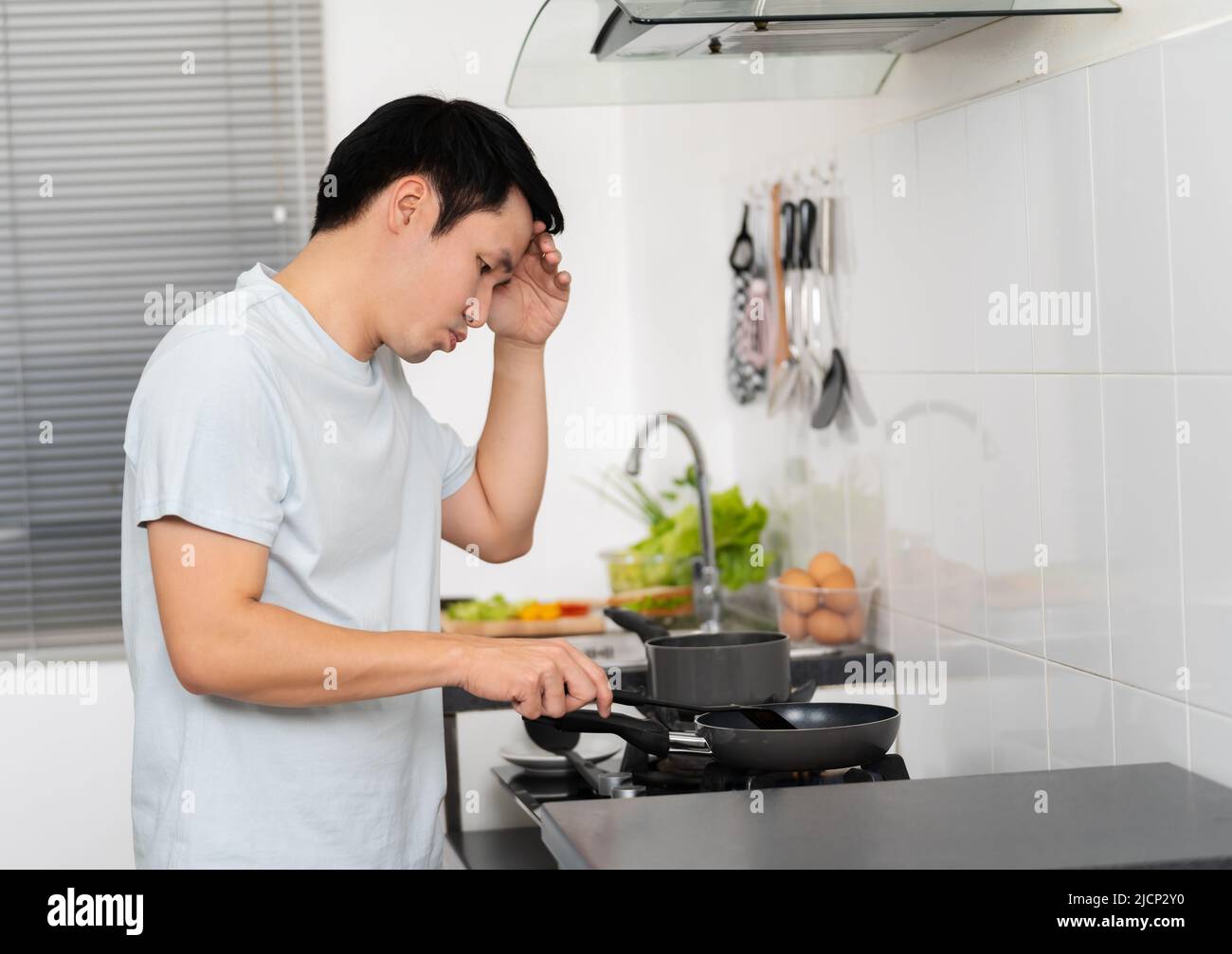 stressed young man cooking and preparing food in the kitchen at home ...