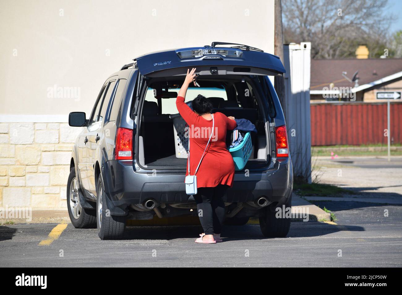 Woman opening the trunk of her SUV and putting a laundry basket of ...