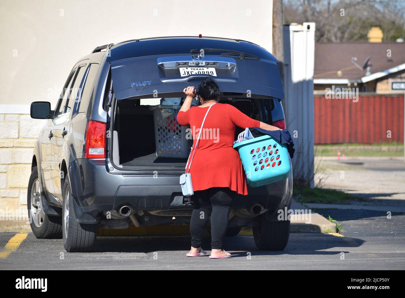 Woman opening the trunk of her SUV and putting a laundry basket of ...