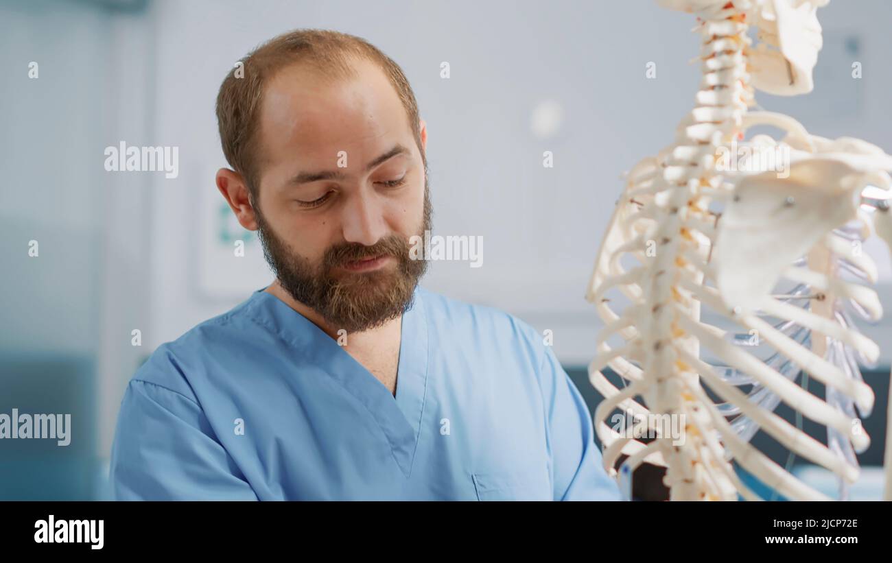 Male osteopath explaining bones on human skeleton exam, pointing at ...