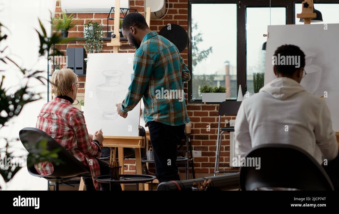 Modern artist analyzing vase drawing by senior woman in art school ...