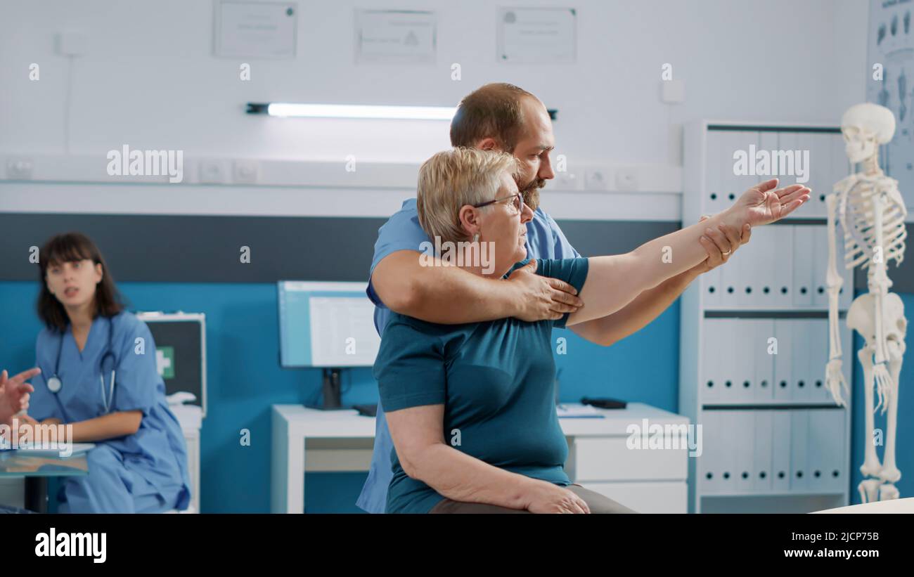 Male osteopath assisting senior woman to stretch arms muscles at ...