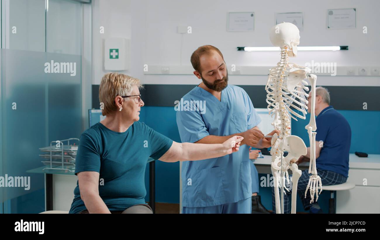 Osteopath explaining orthopedic diagnosis on human skeleton to elder ...