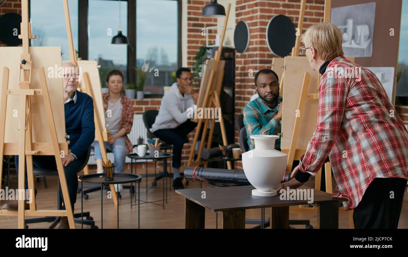 Senior teacher explaining drawing technique to diverse team of students ...