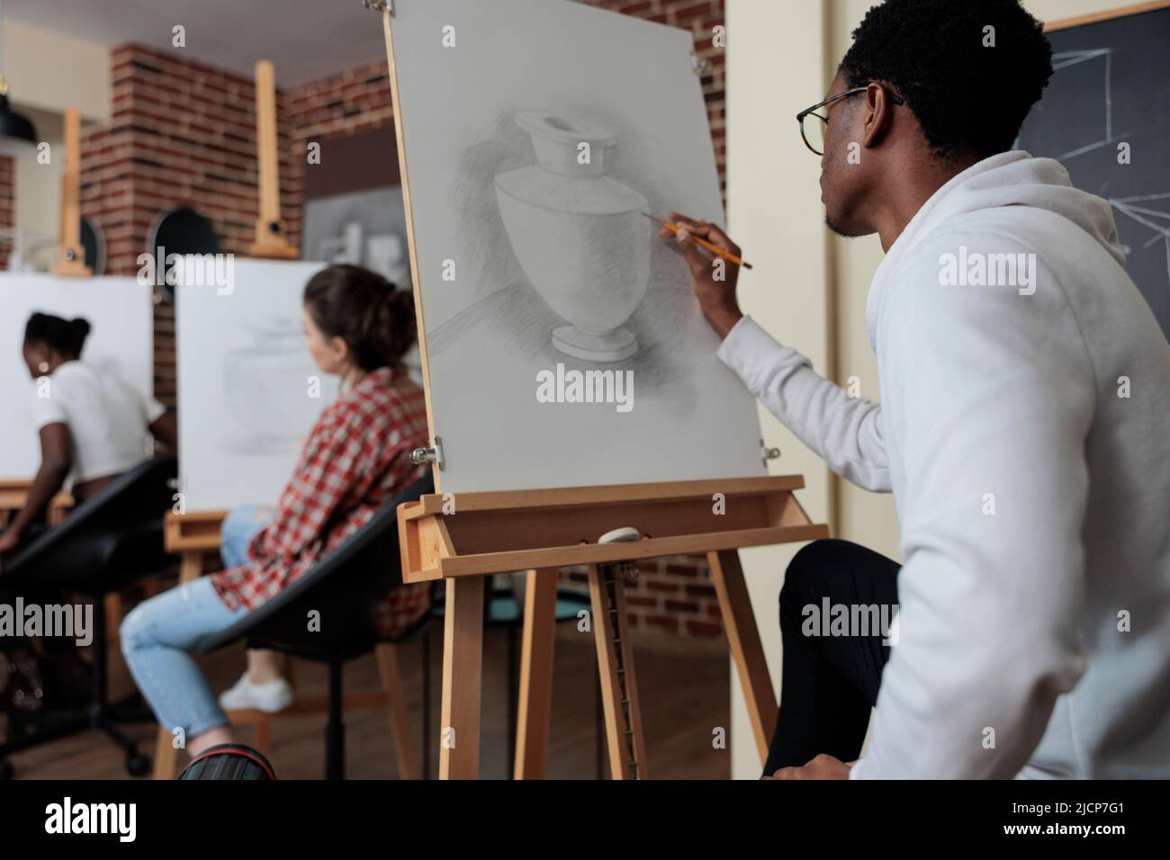 Creative student sitting in front of white canvas drawing vase model ...