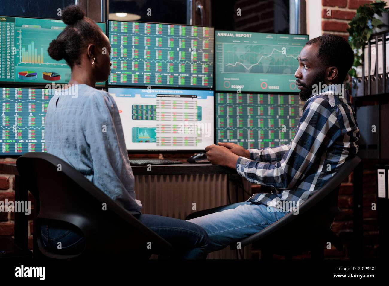 Sales consultants sitting at multi monitor workstation while discussing ...