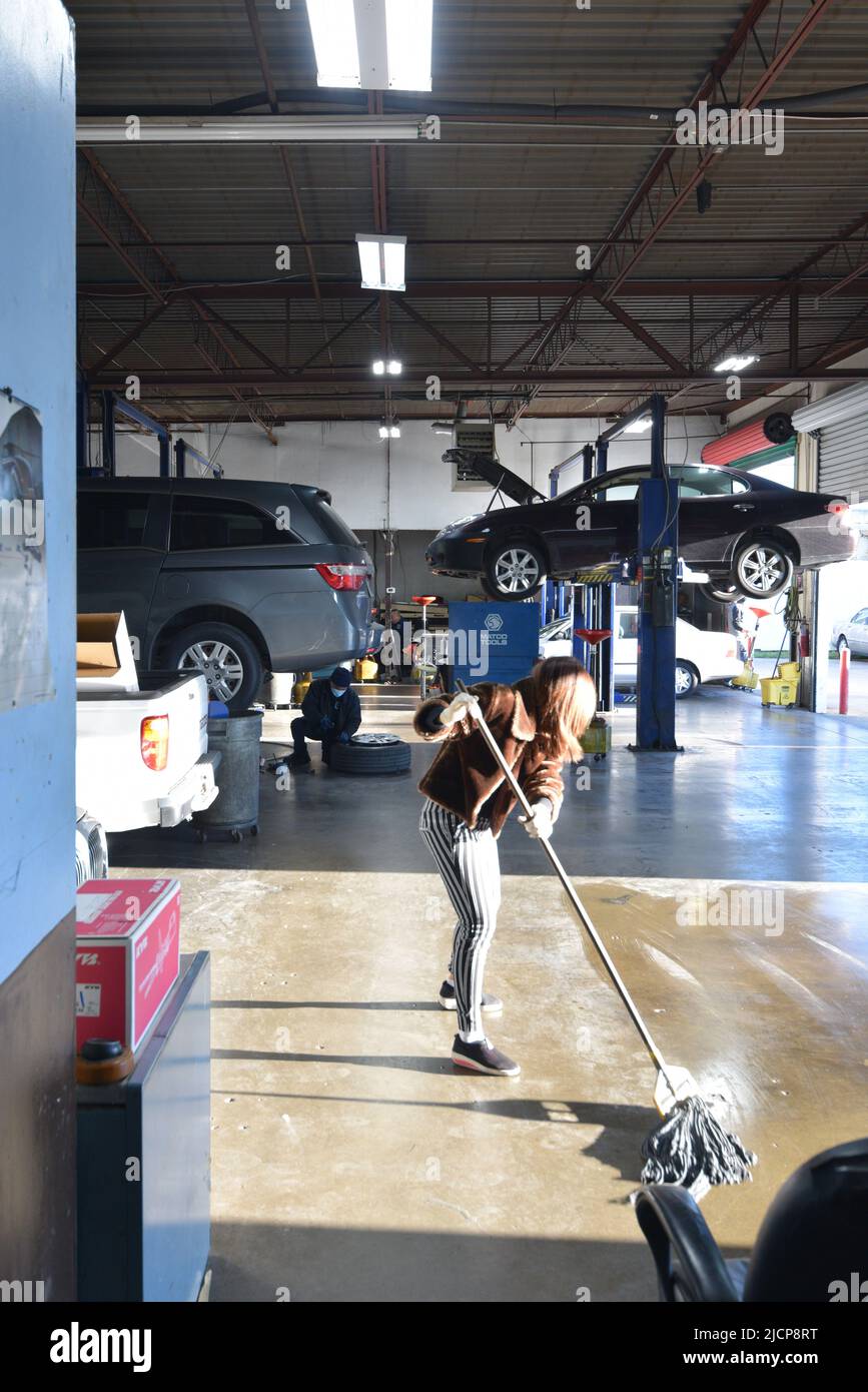 Woman mopping floor in an area of a car repair shop, cars on a rack or ...
