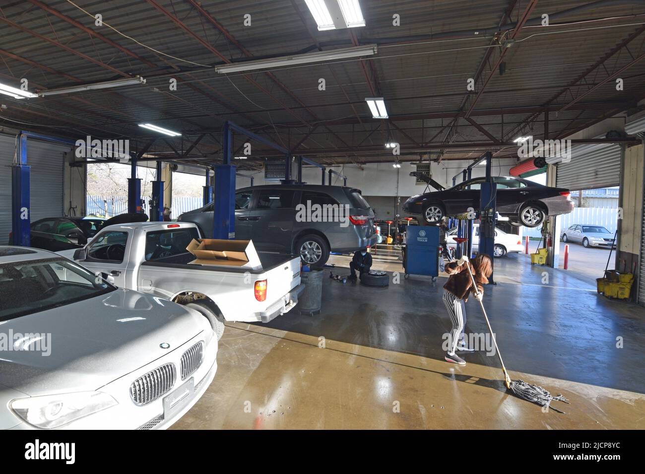 Woman mopping floor in an area of a car repair shop, cars on a rack or ...