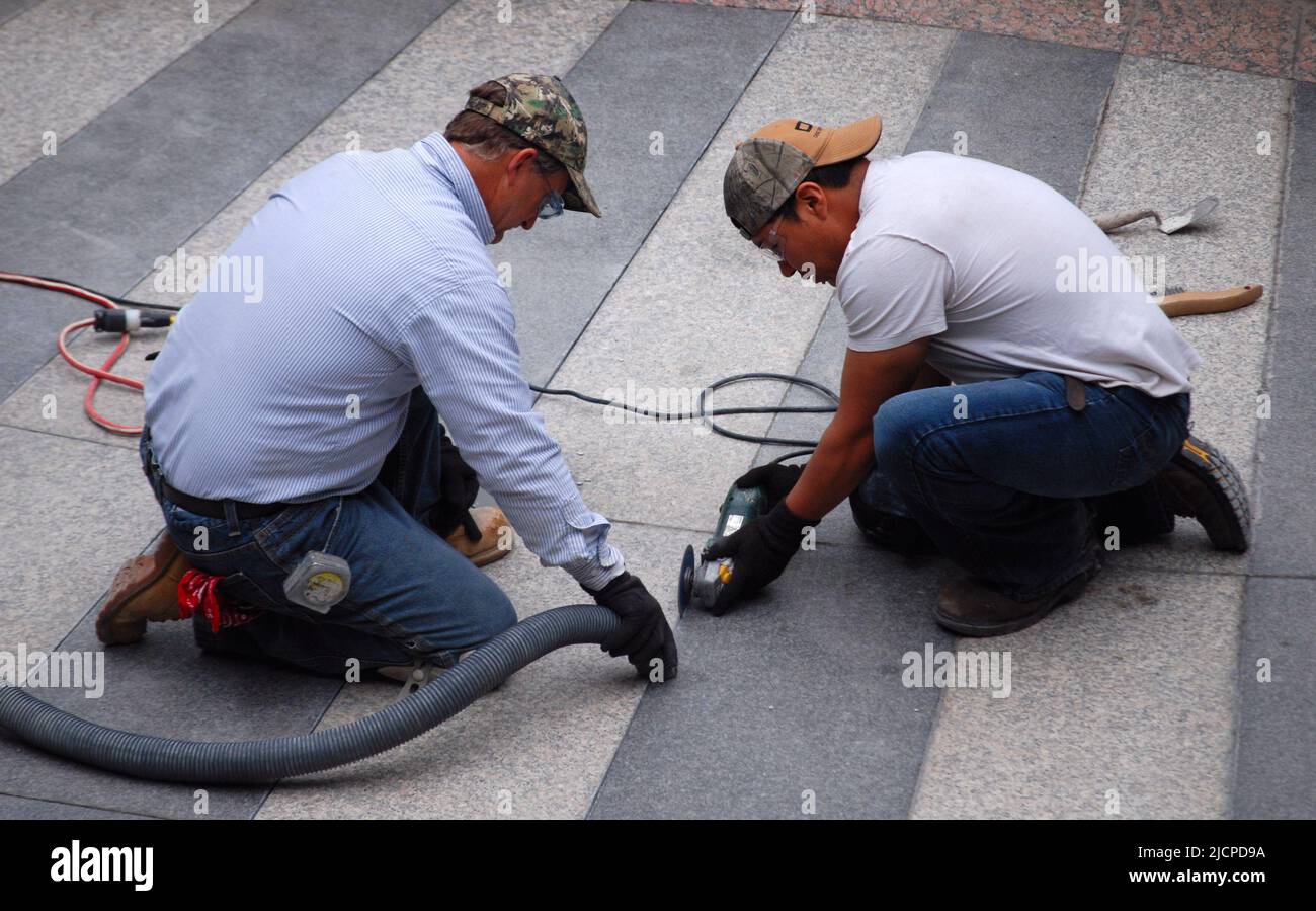 Workers doing manual labor as they work on a large tile floor at the ...